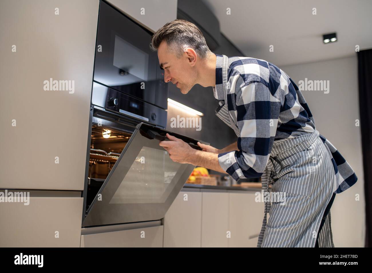 Satisfied man opening looking into oven Stock Photo - Alamy