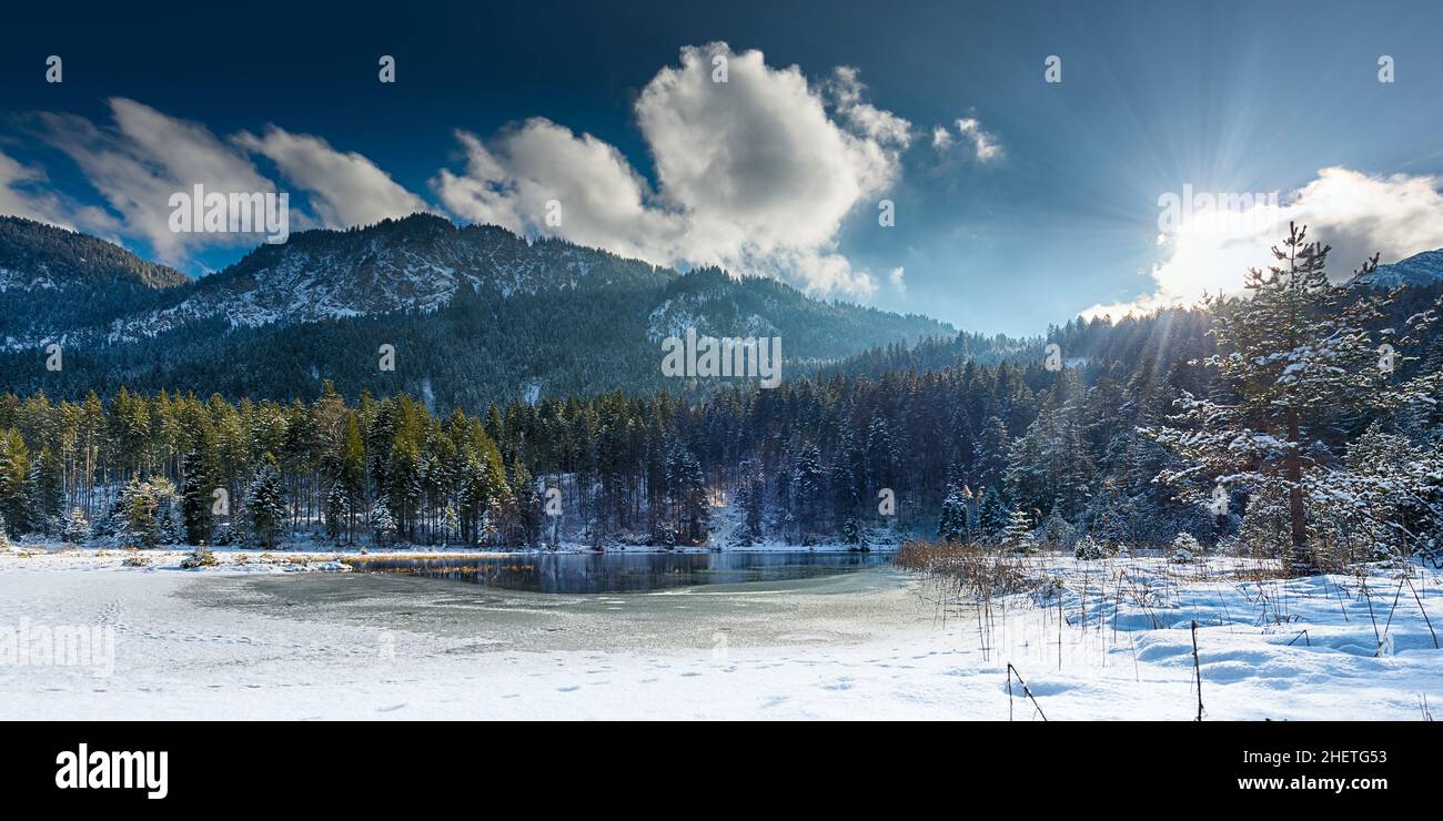 small frozen lake in austrian alps with sun shining through clouds ...