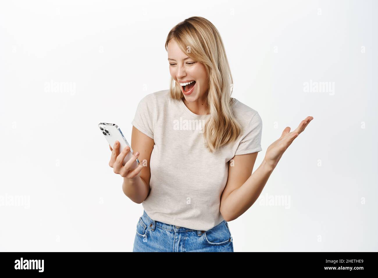 Happy blond girl winning on mobile phone app, watching smartphone and ...