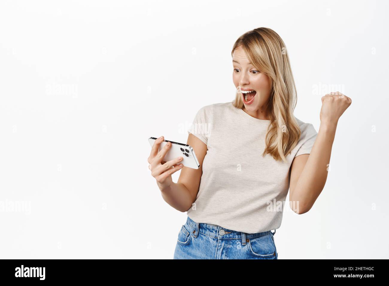 Blond girl winning, celebrating with mobile phone in hands, achieve ...