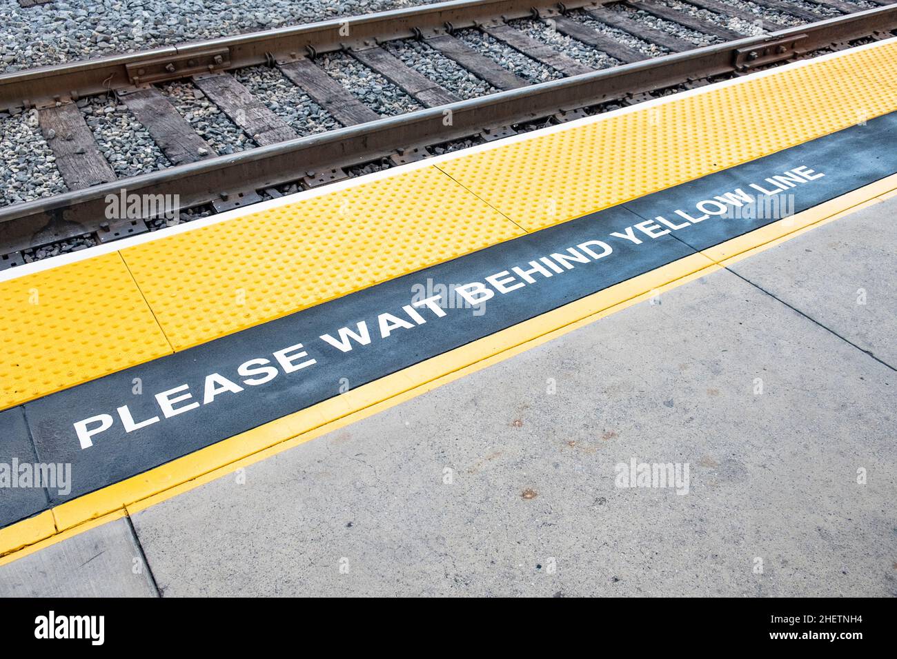 train platform with sign please wait behind the yellow line and yellow ...