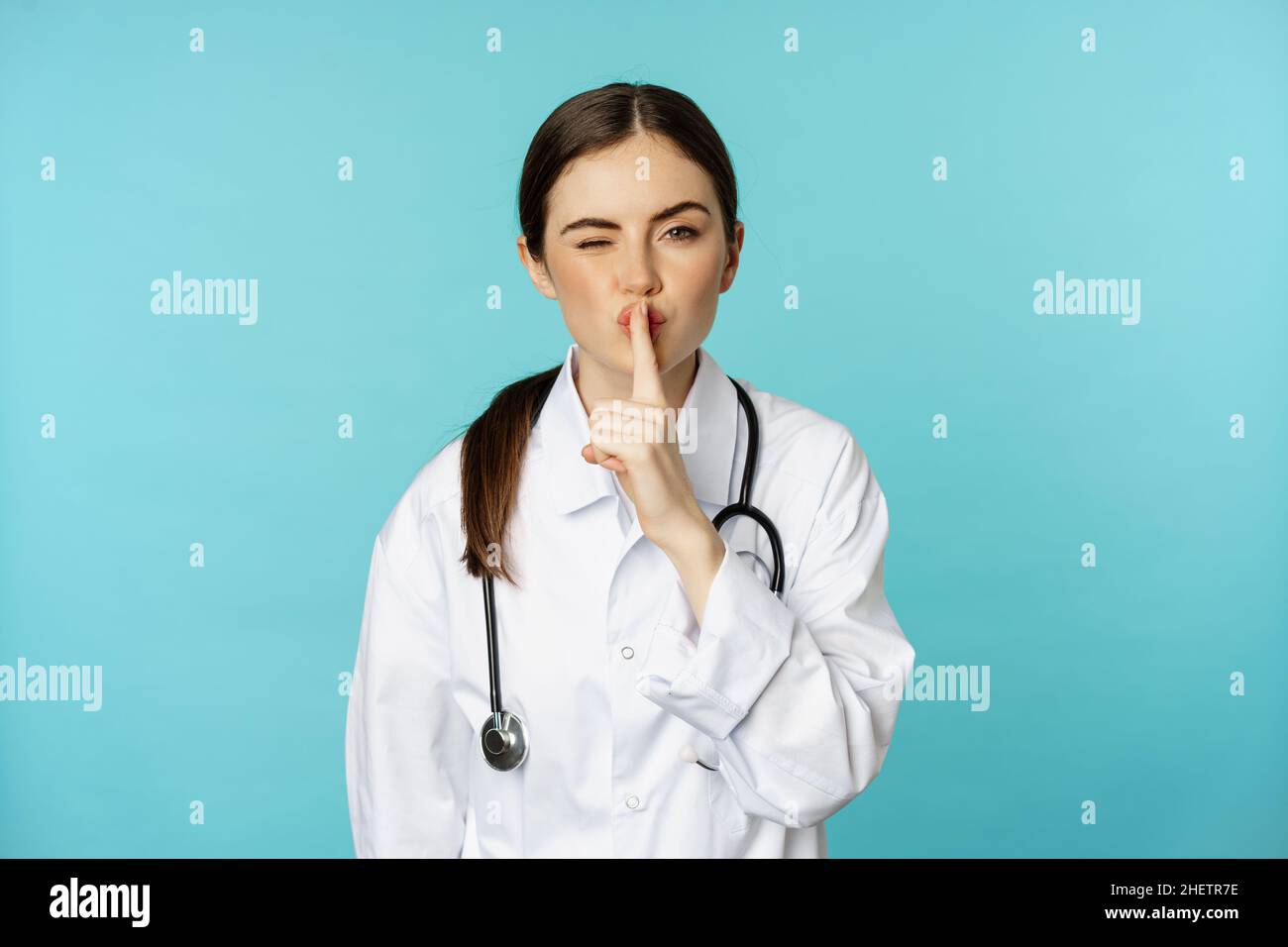 Smiling cute doctor woman, shush, press hush shh sign with finger ...