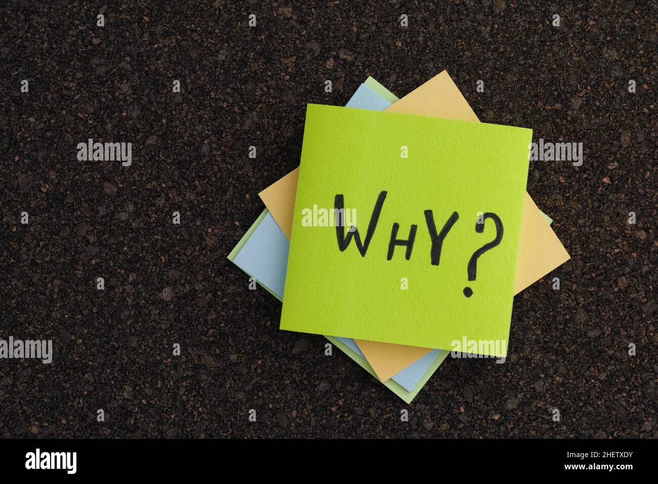 A stack of colorful sticky notes with the Why question on a cork board ...