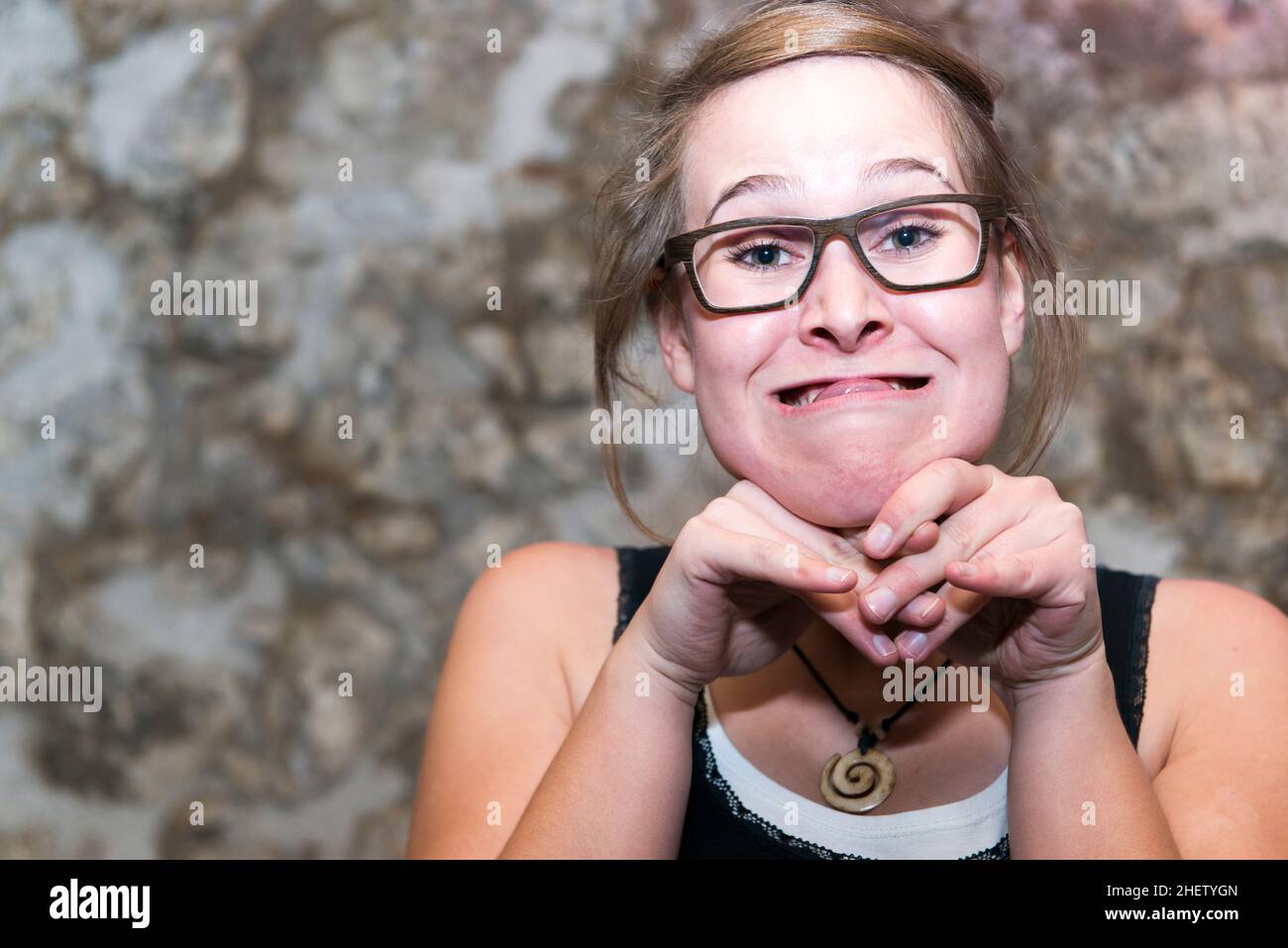 Young woman goofing around pulling faces with her hands under her chin ...