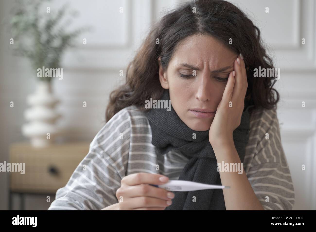 Unhealthy hispanic female looking at thermometer with sad face while ...