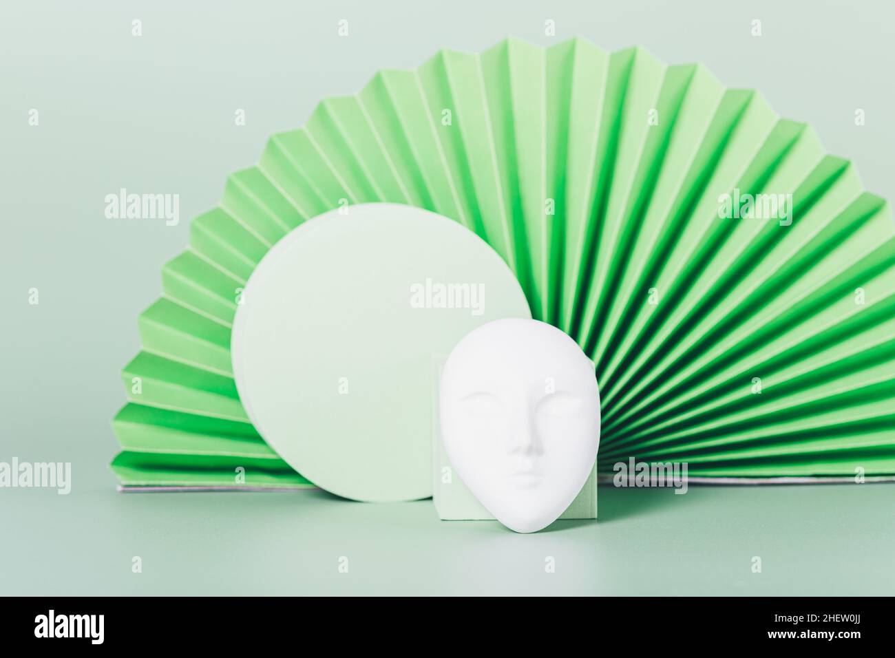 Round pedestal with paper origami fan and gypsum face mask on light green background Stock Photo ...