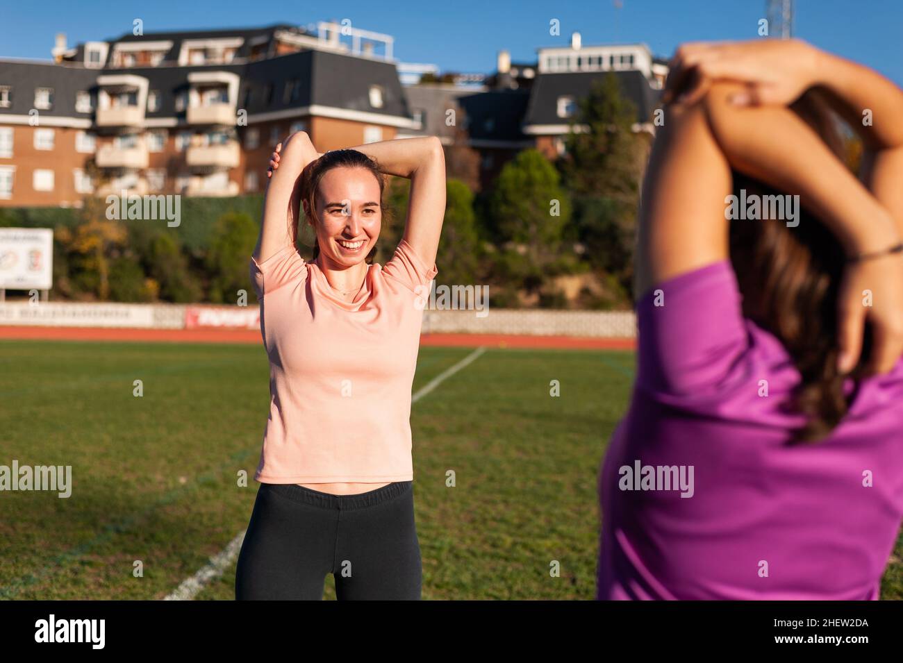 two young women doing stretching on the grass of a running track before ...