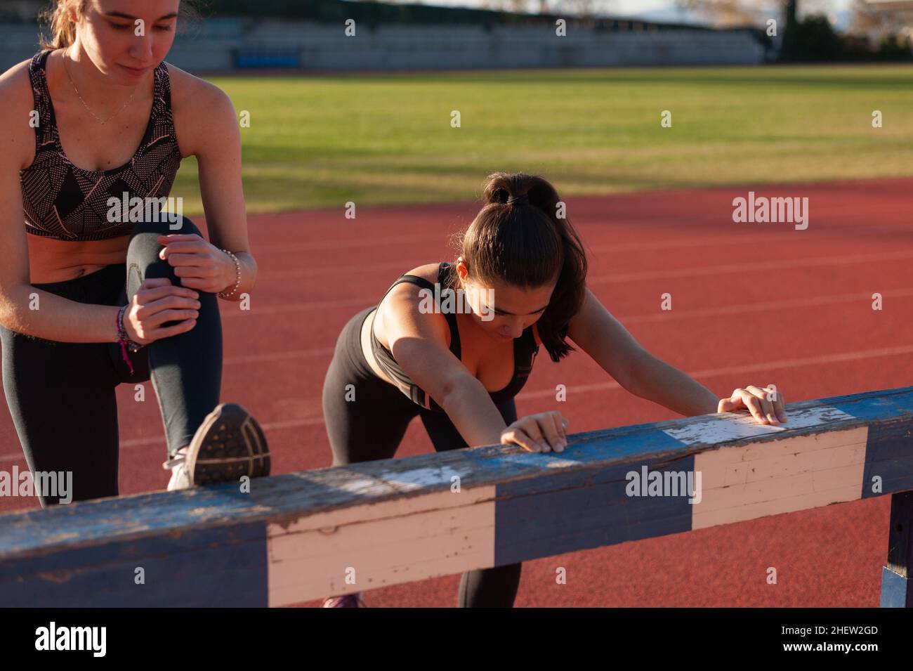 two young women doing stretching on the grass of a running track before ...