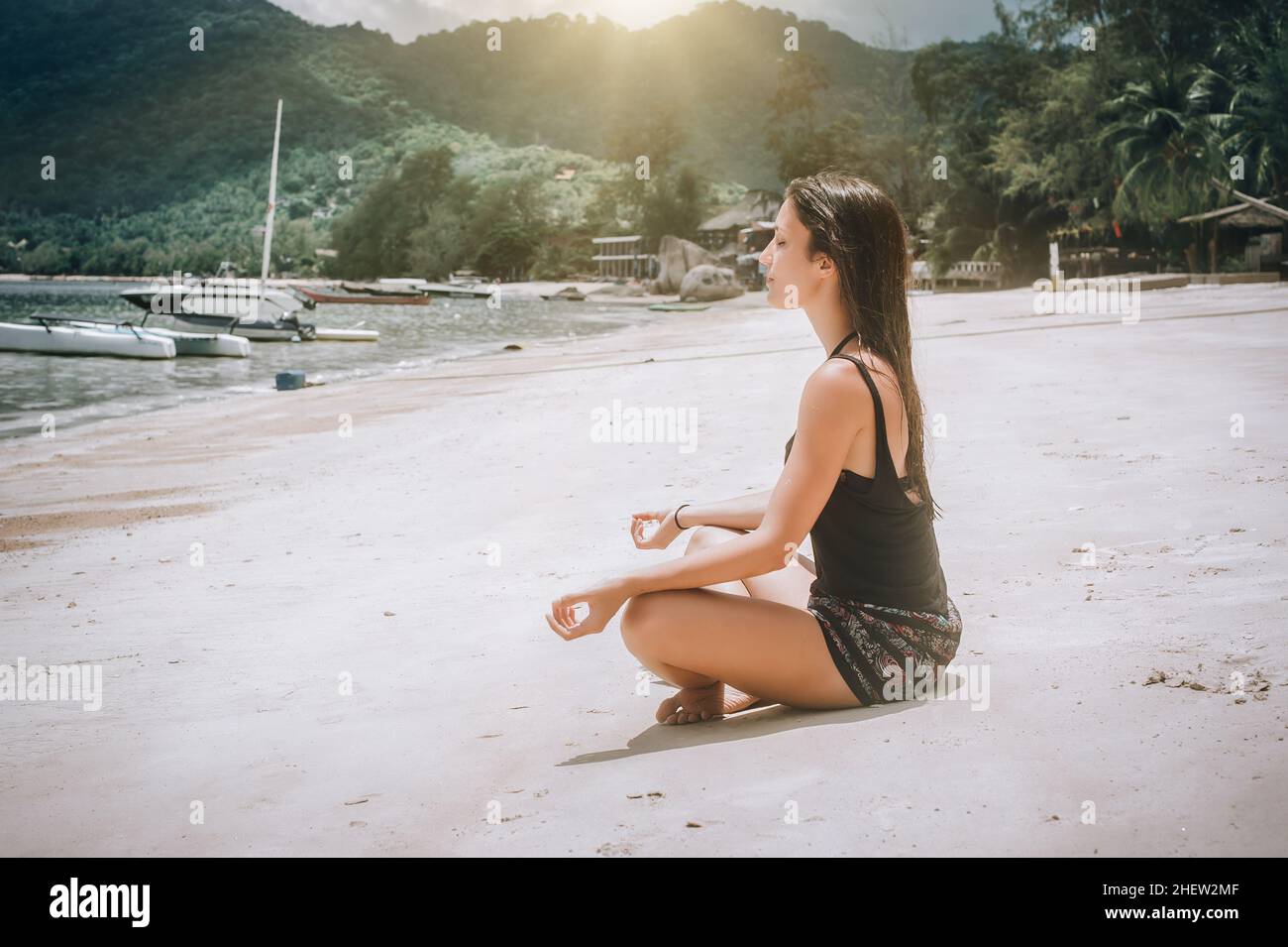 Young woman doing yoga pose on beach in summertime in lotus position ...
