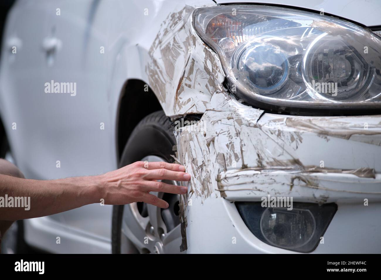 Driver hand examining dented car with damaged fender parked on city ...