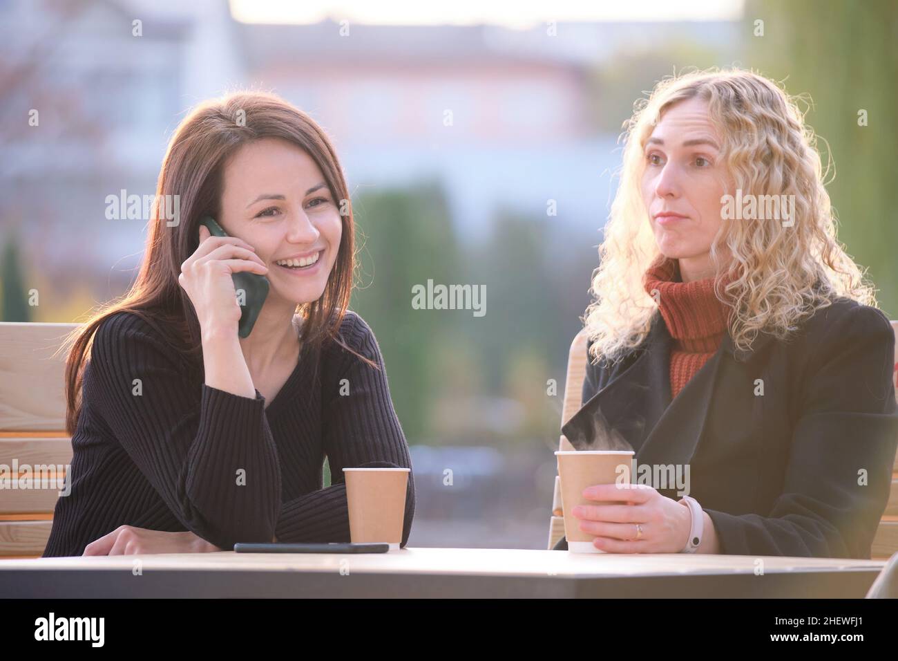 Sad woman being ignored by her friend sitting at street cafe outdoors ...