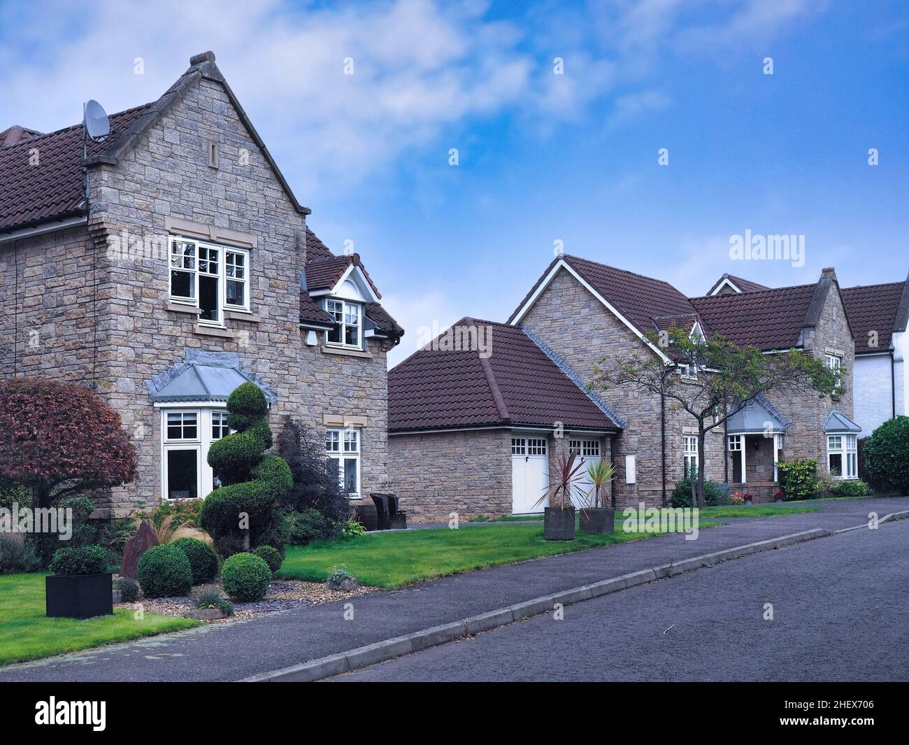 Suburban residential street with two story stone houses with gables and ...