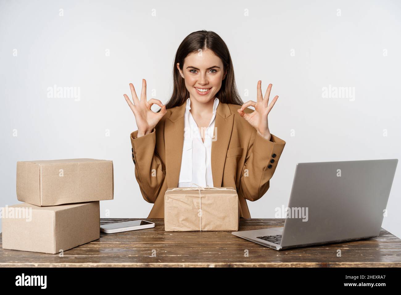 Woman small business owner, sitting at table with laptop, packing boxes ...