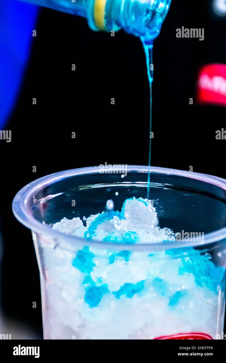 Pouring a sweet blue syrup into a transparent plastic glass with cold ...