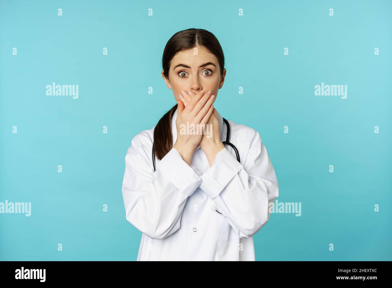 Shocked and concerned woman doctor, clinic worker, covering mouth with ...