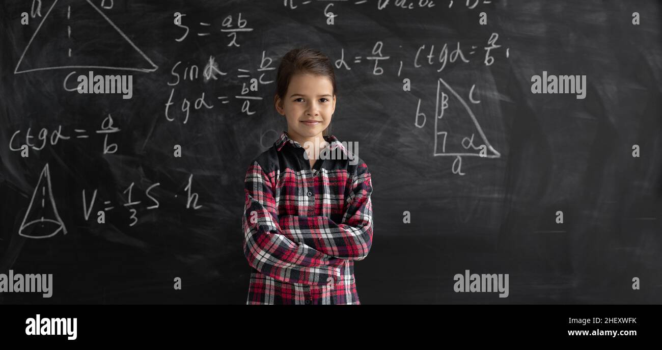a schoolgirl girl in a shirt stands at the chalk board against the ...