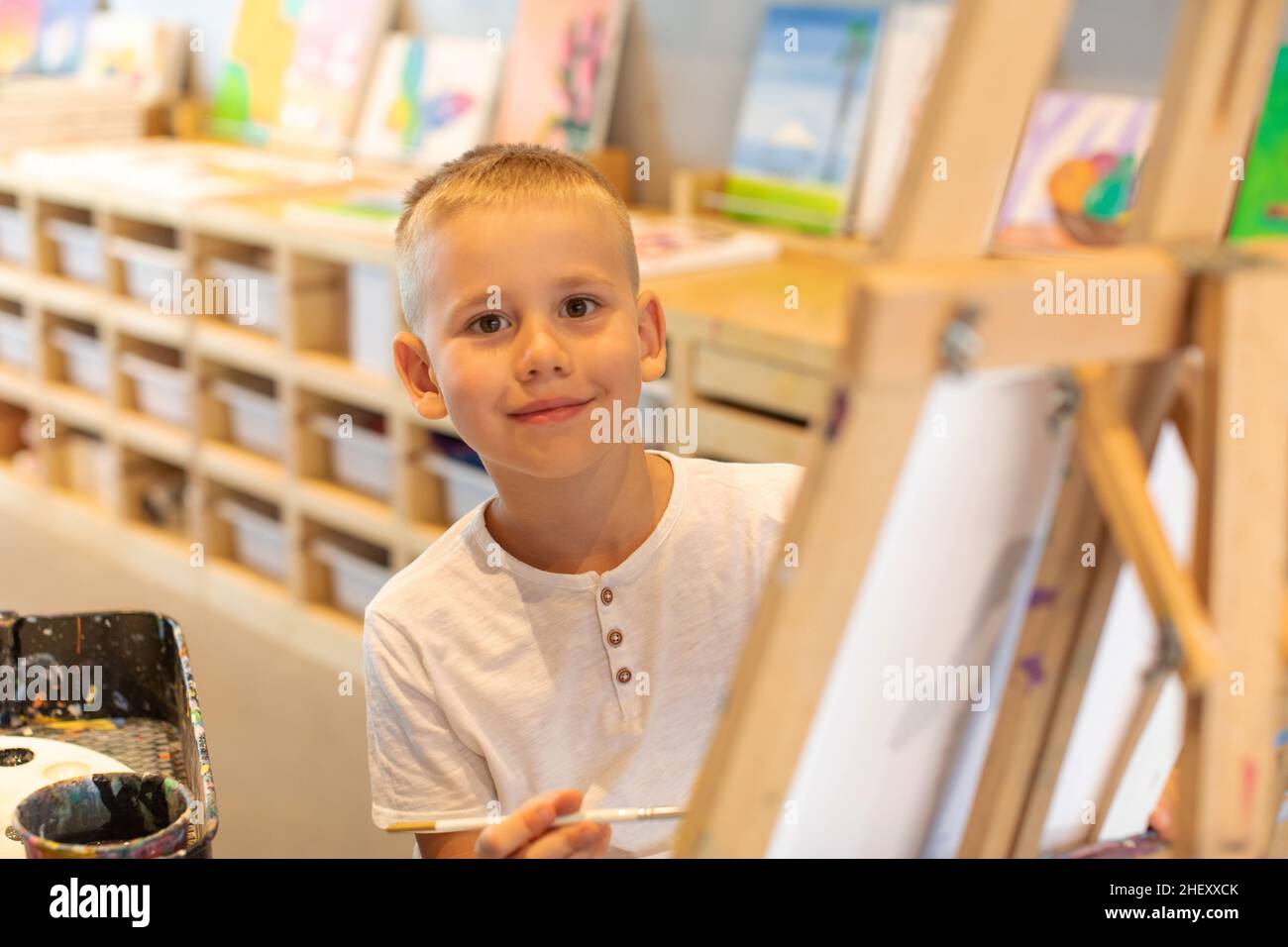 Smiling blond boy draws on canvas in the workshop. Drawing lessons for ...