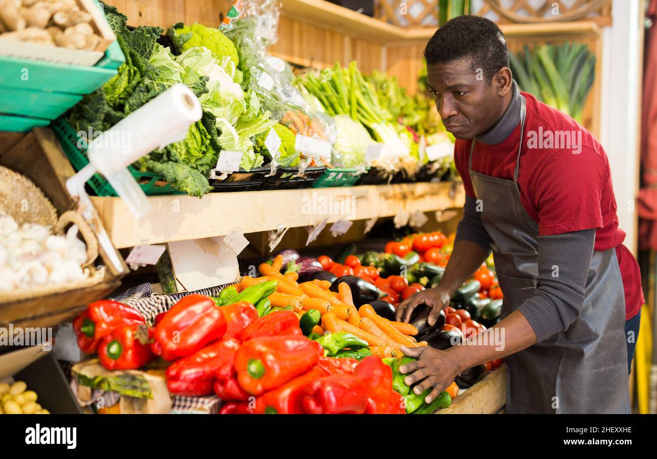 Salesman filling counter with vegetables and fruits Stock Photo - Alamy
