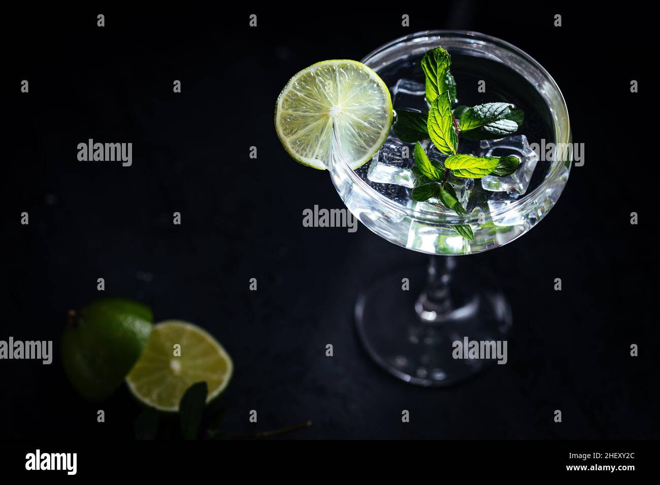 Gin tonic in cocktail glass with ice, mint leaves and lime on a dark ...