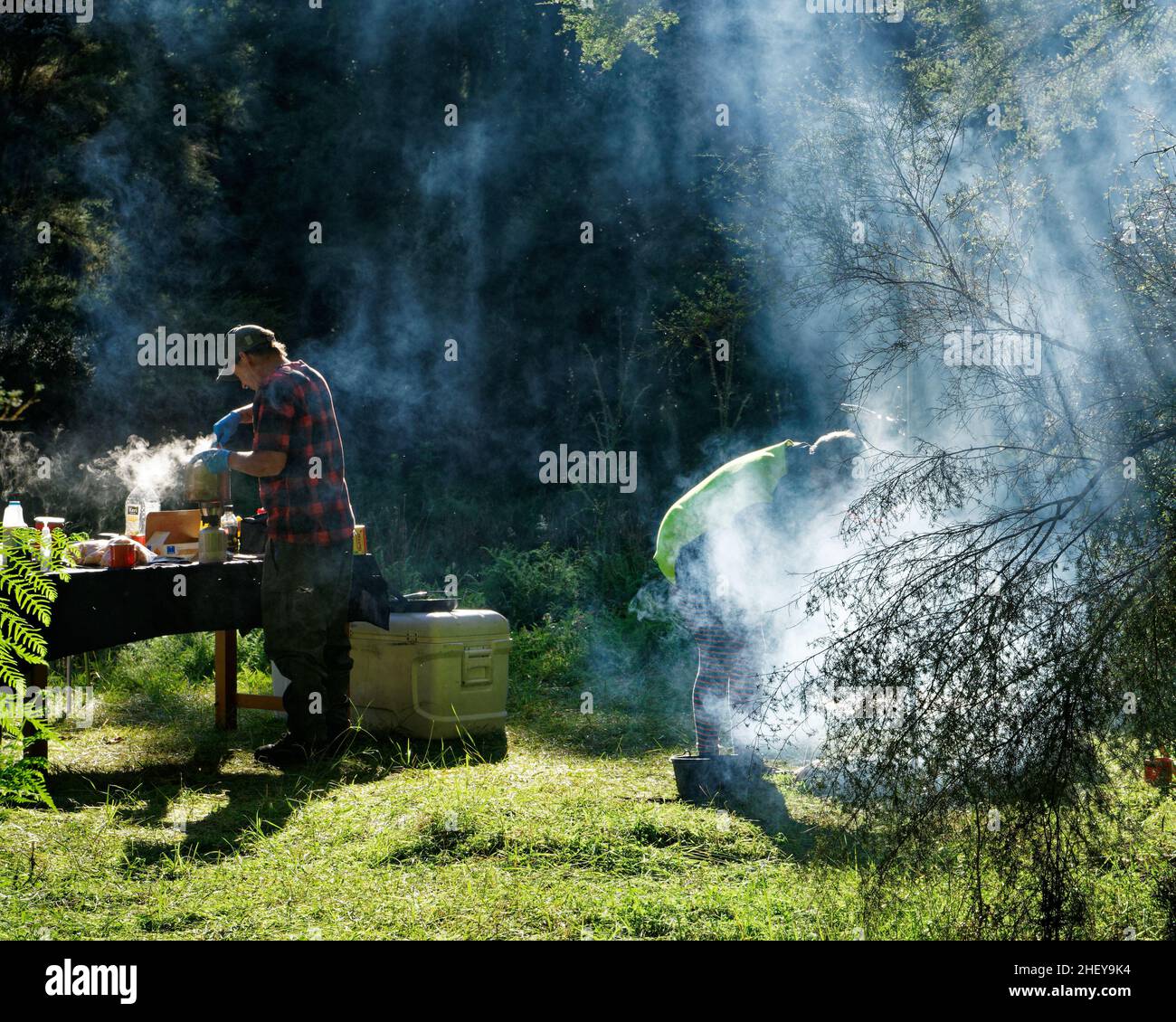 Two people preparing breakfast on an open fire, back country camping ...