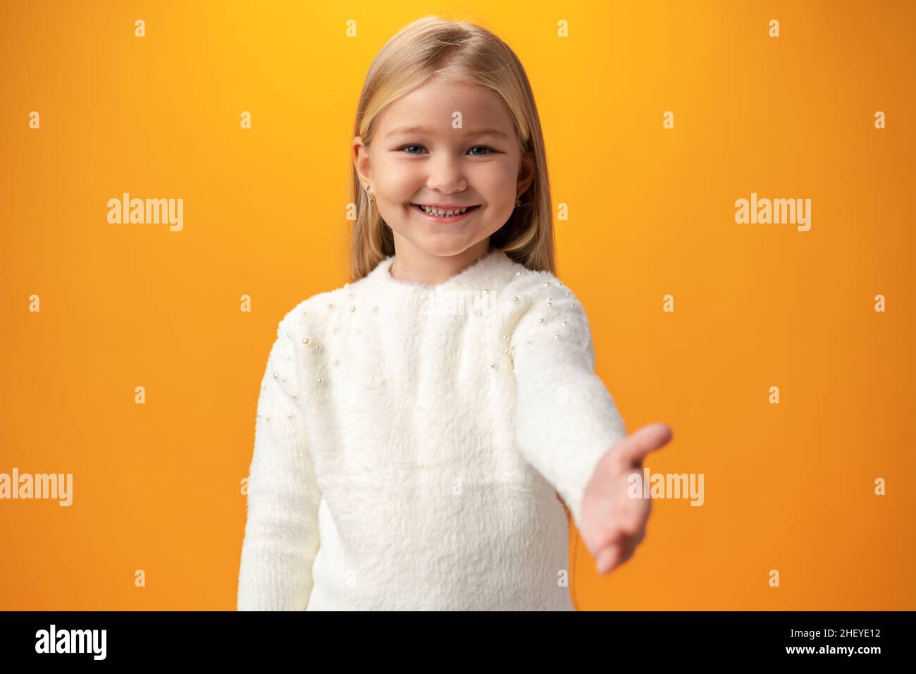Happy cute child girl giving hand for greeting against yellow ...