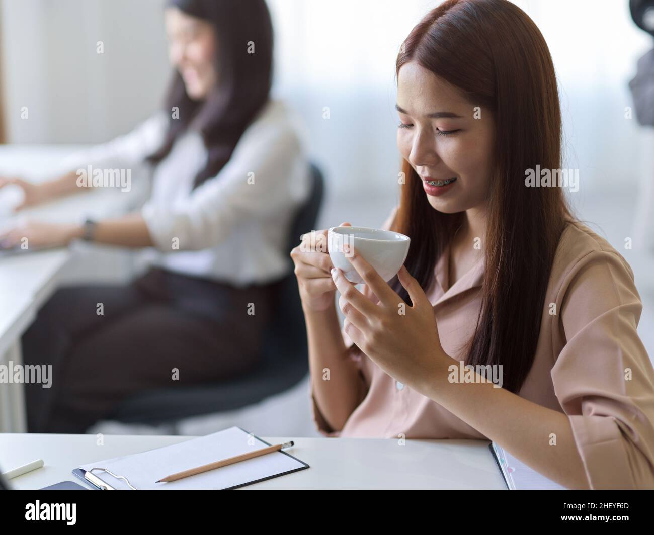Asian young female employee sipping hot tea at her office desk ...