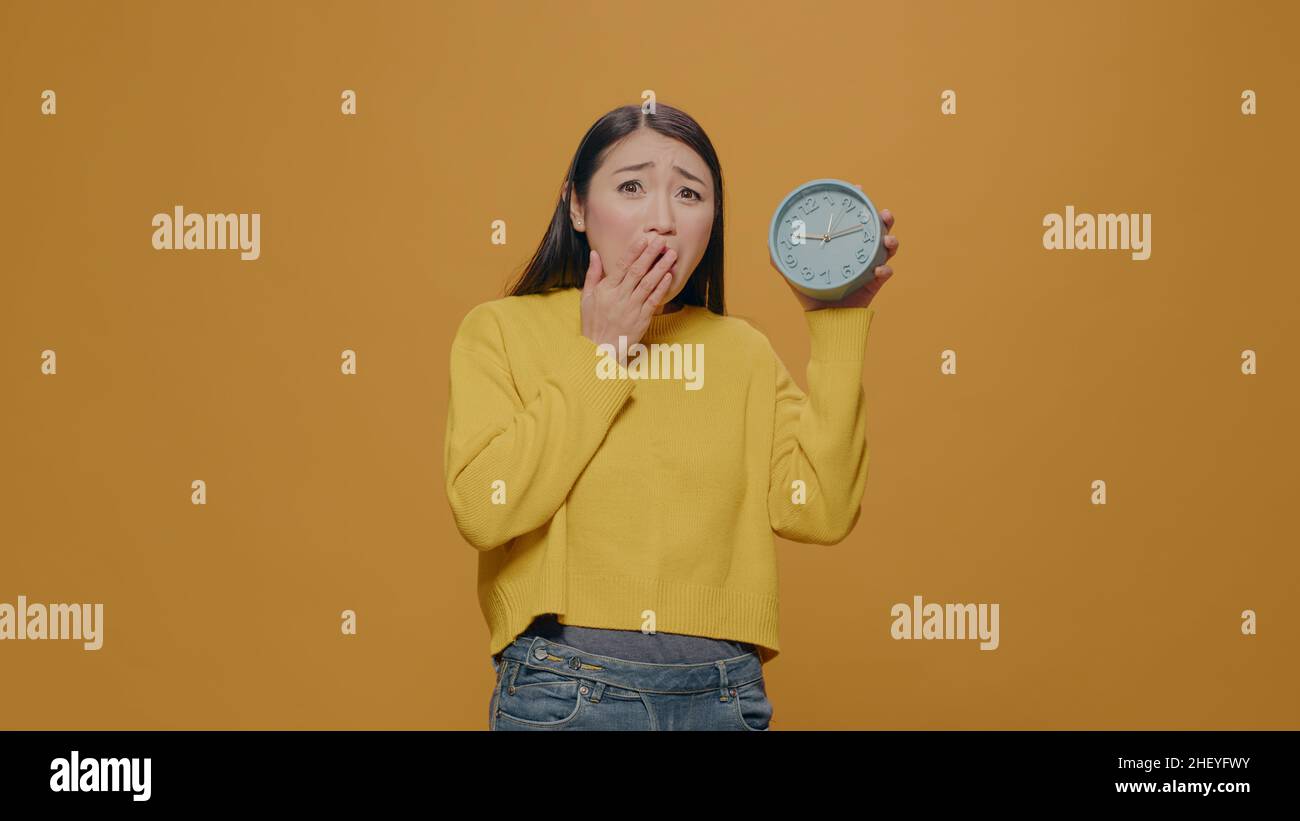 Asian woman with anxiety checking time on clock in studio, running late ...
