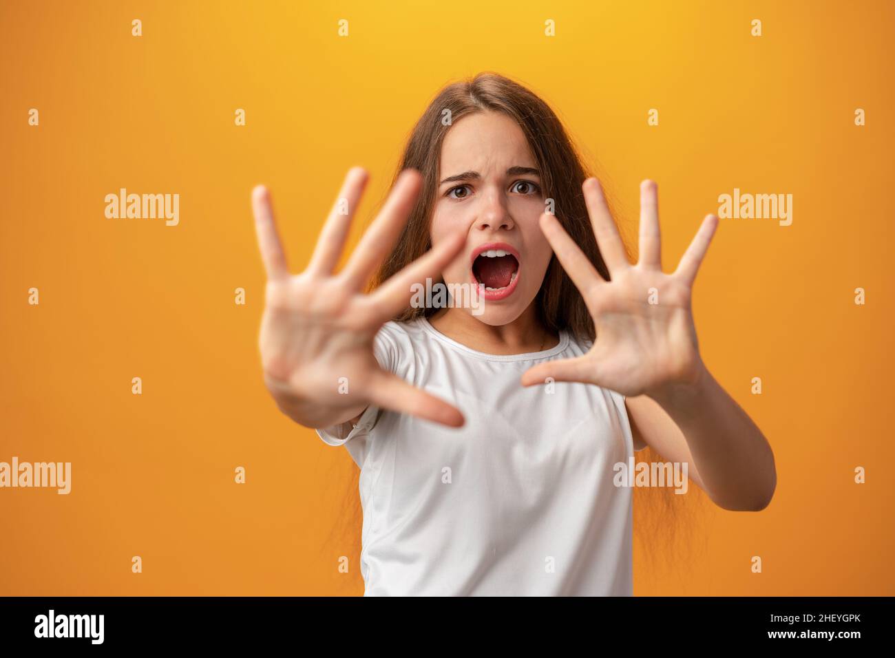 Scared young teen girl showing stop gesture against yellow background ...