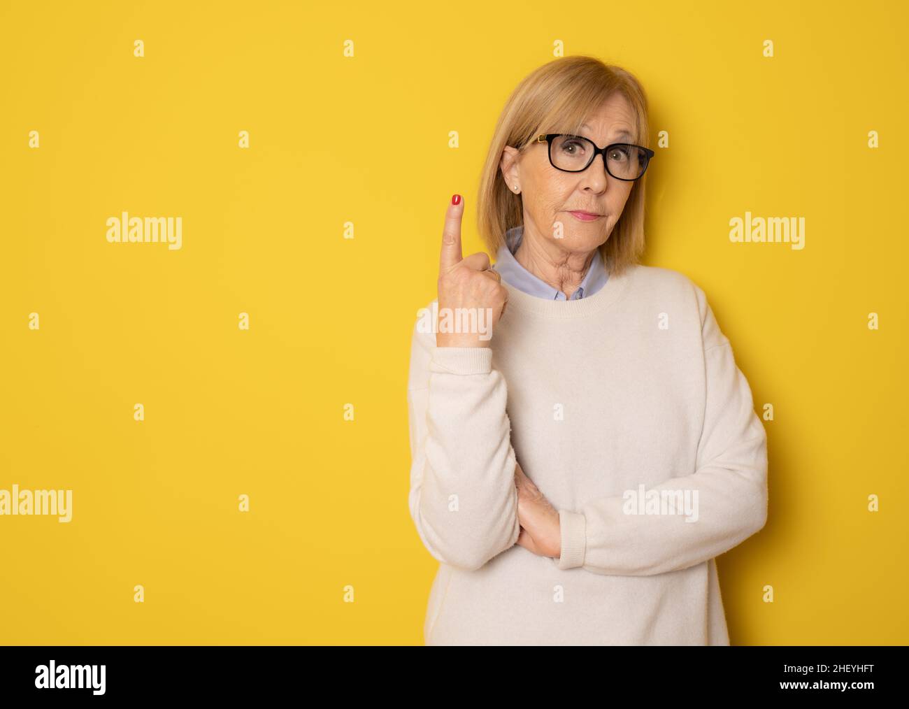 Portrait of old strict woman wearing glasses pointing up with finger ...
