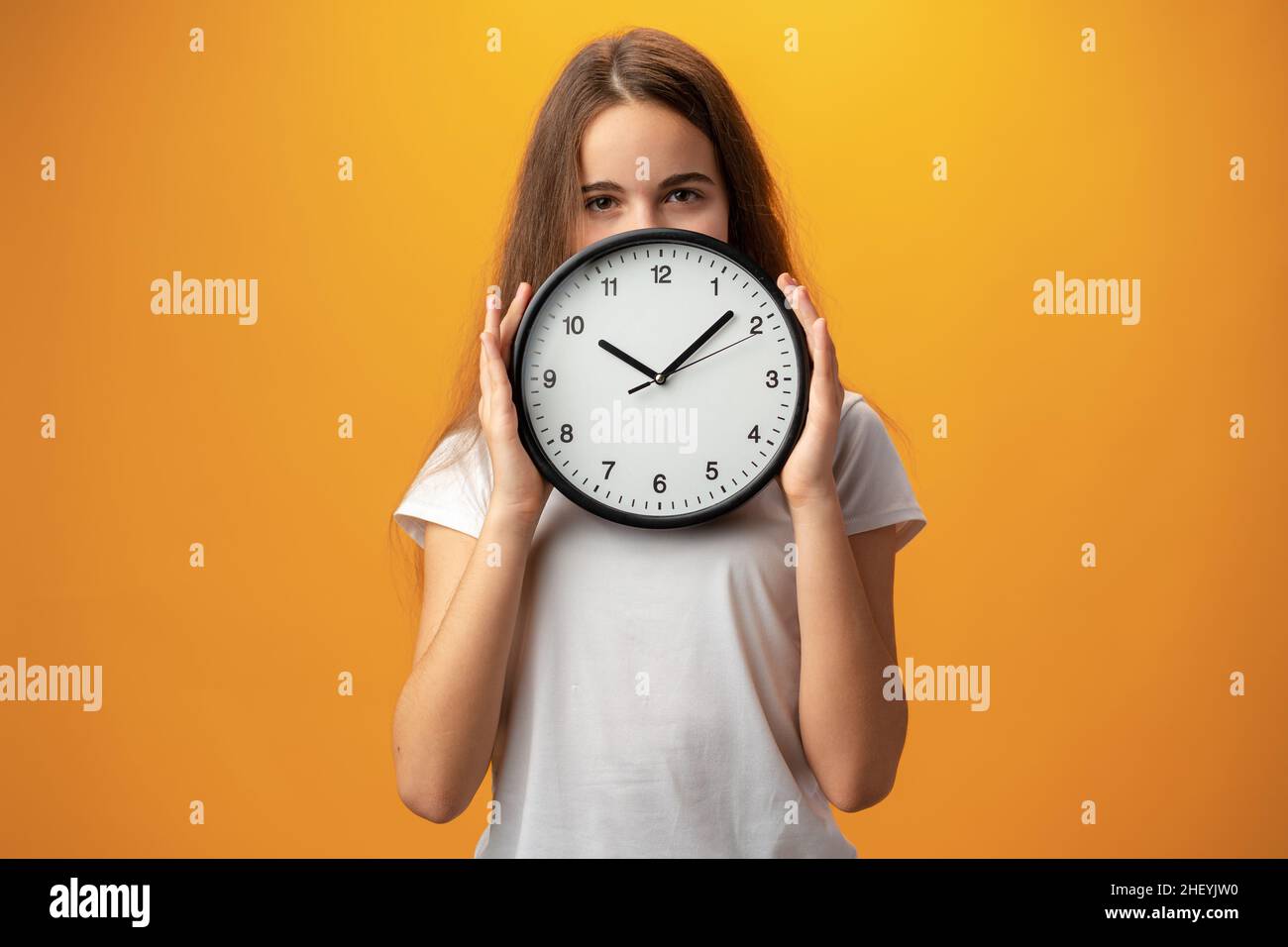 Beautiful teen girl holding wall clock over yellow background Stock ...