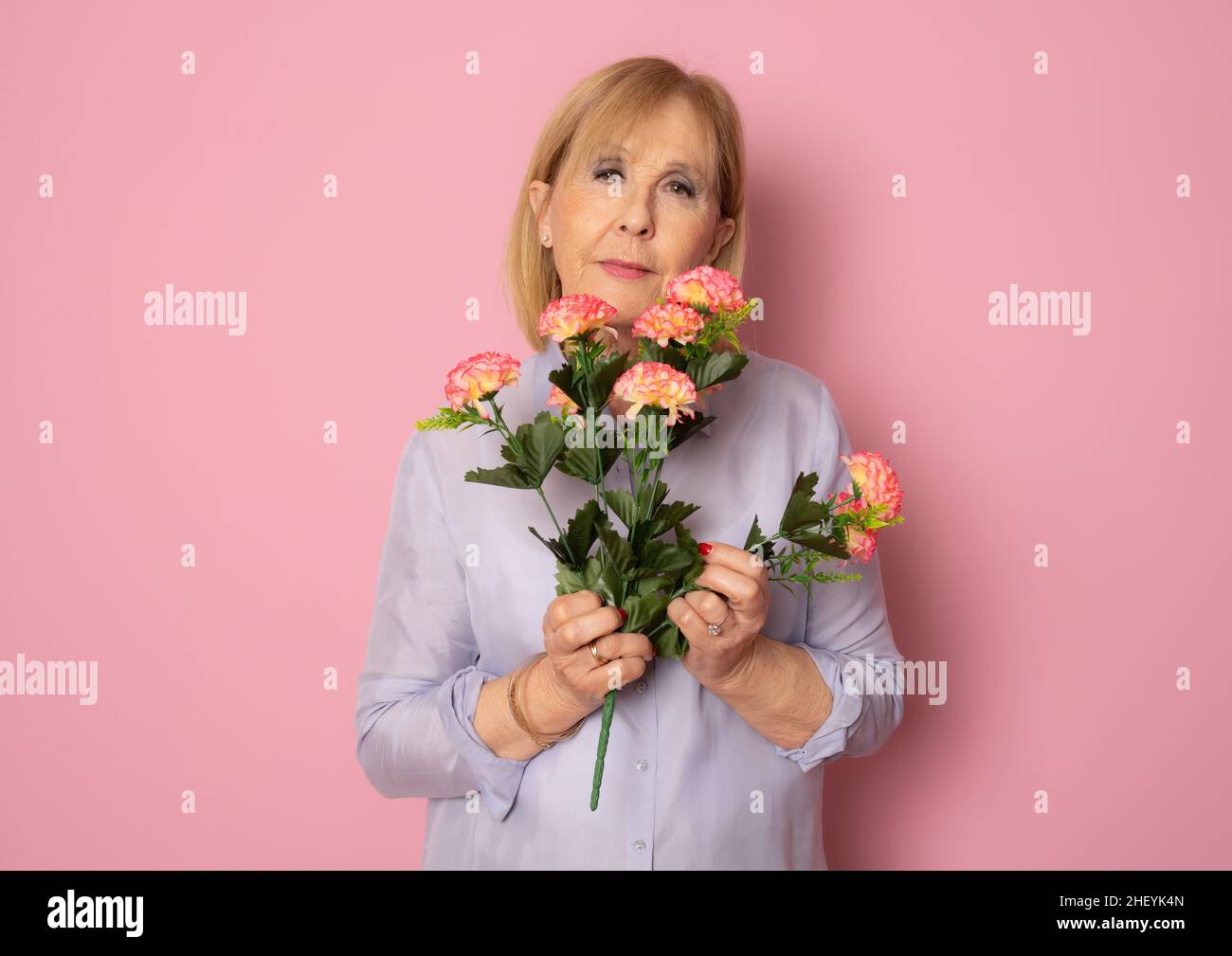 Happy senior woman with bouquet of flowers standing isolated over pink ...