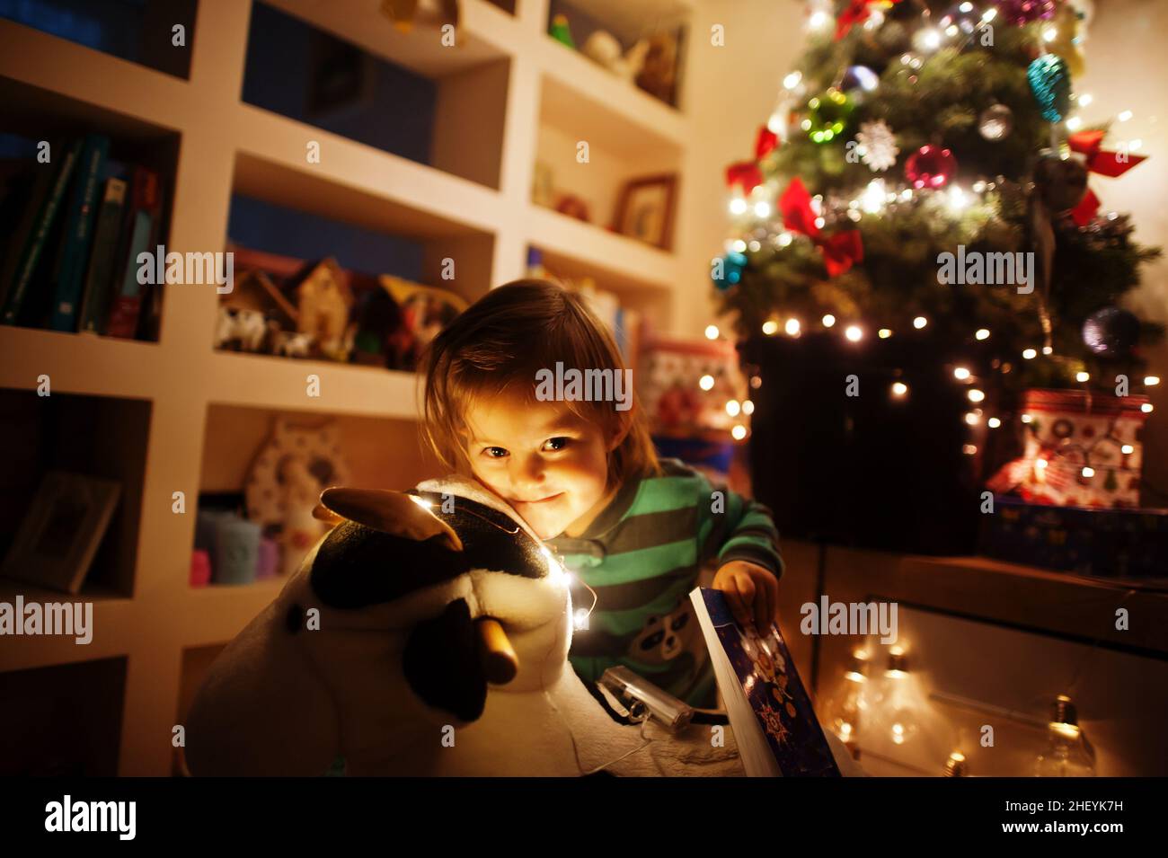 Baby girl on rocking cow toy against Christmas tree with shining ...