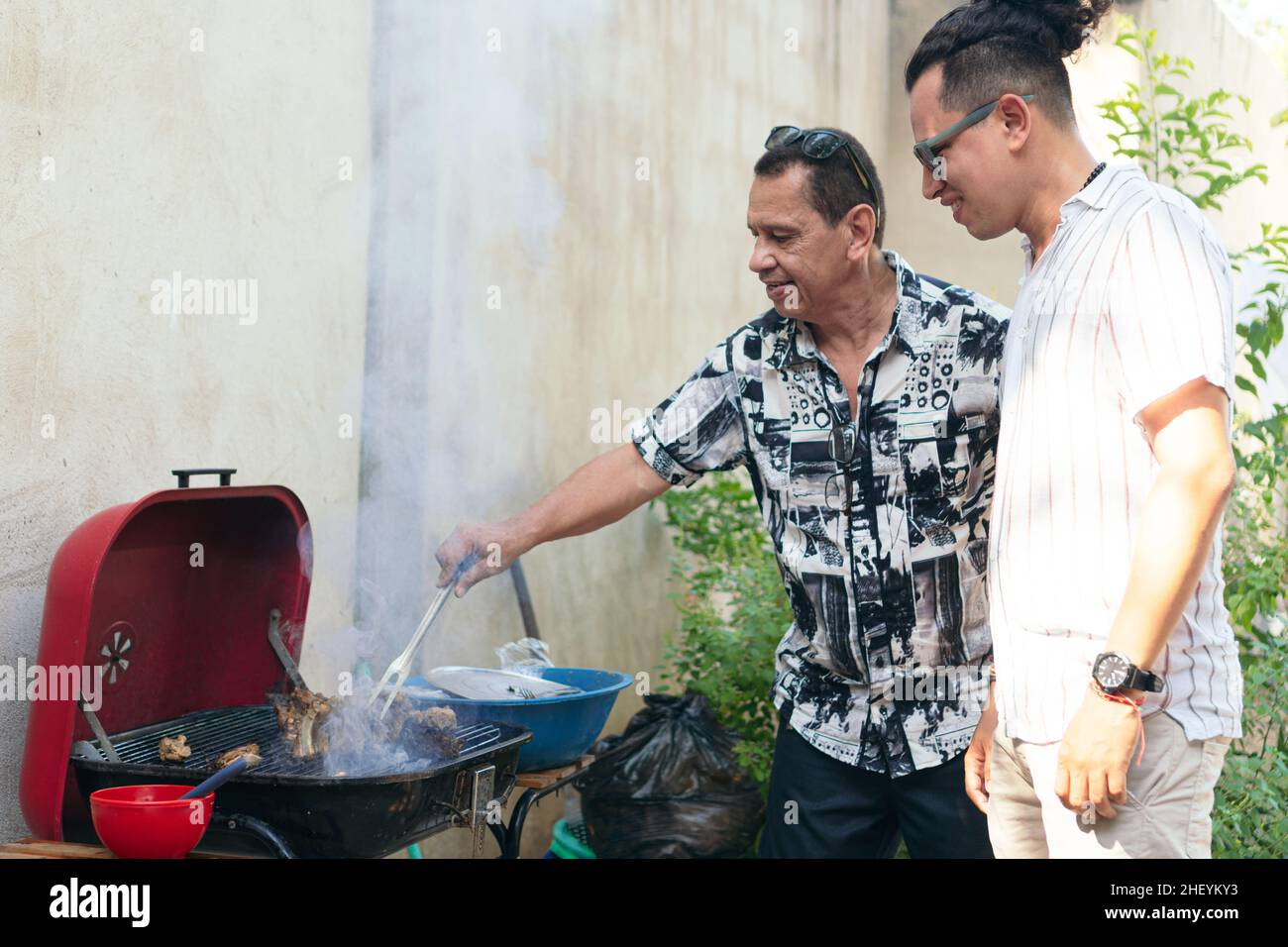 Older man preparing meat on a barbecue grill for his family's lunch in ...