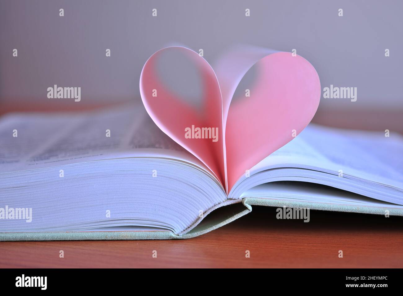 An unfolded book on a table with a pink heart made of pages. Blurred ...