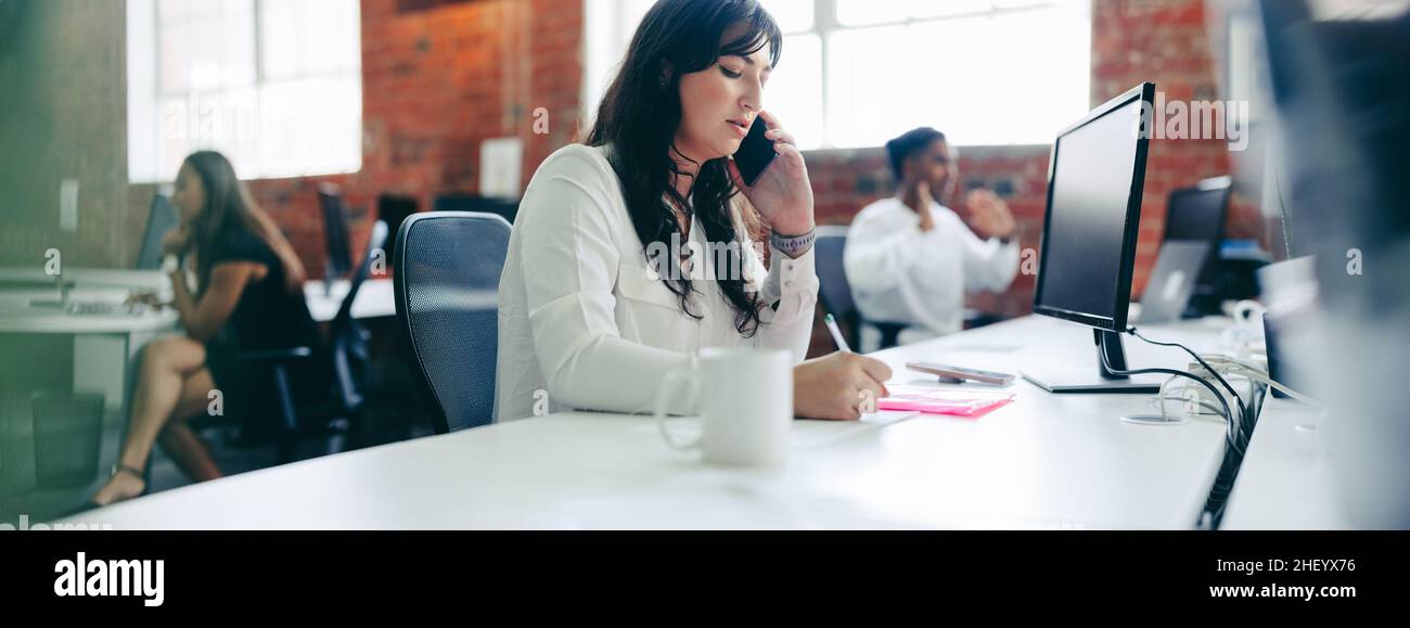 businesswoman making notes while speaking on a phone call. Creative ...