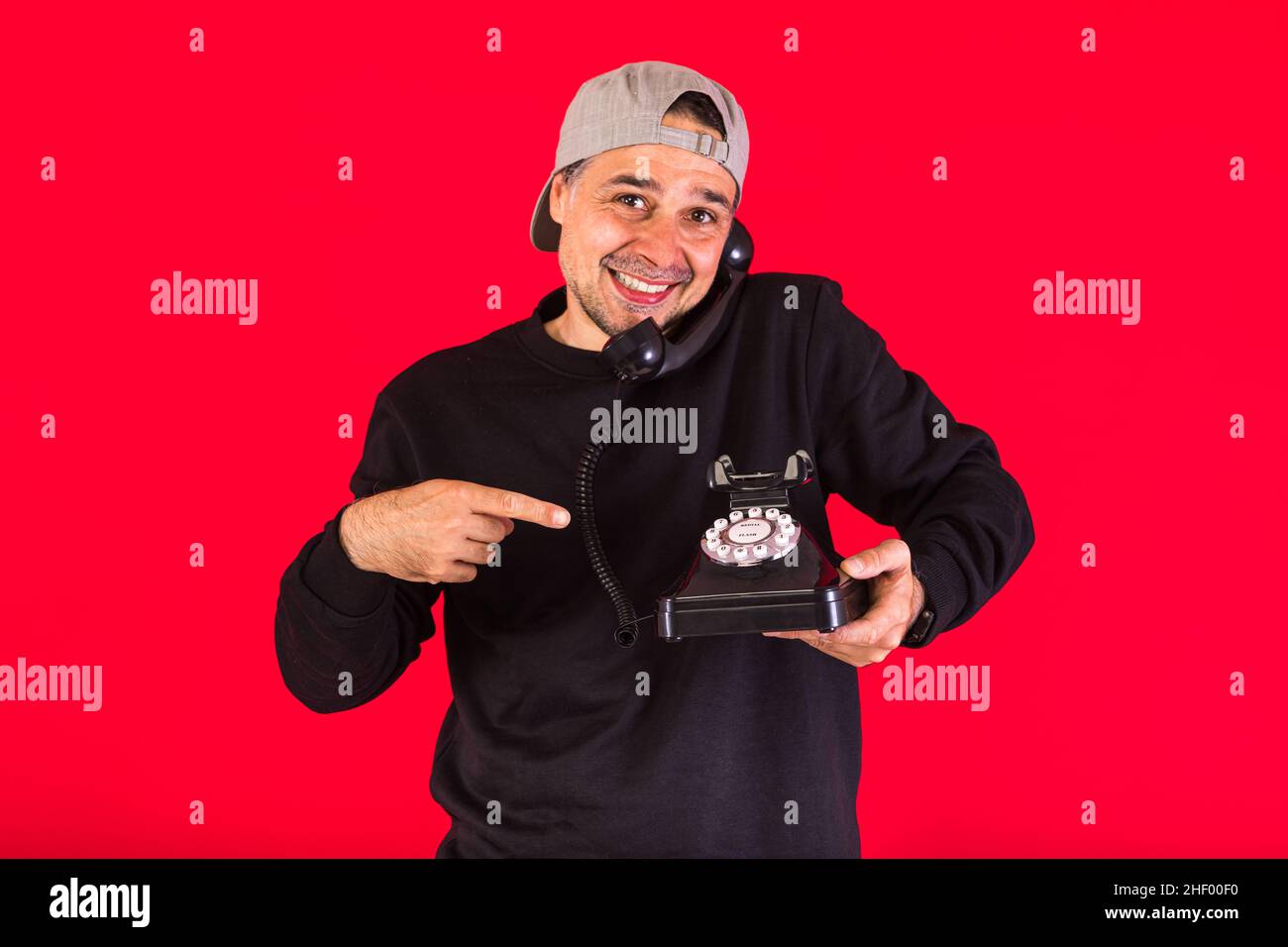 Man in a cap dressed in black, answers a call with a retro phone from ...