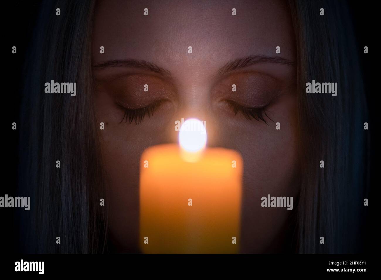 Close-up of woman`s face with eyes closed in the dark behind a blurred ...