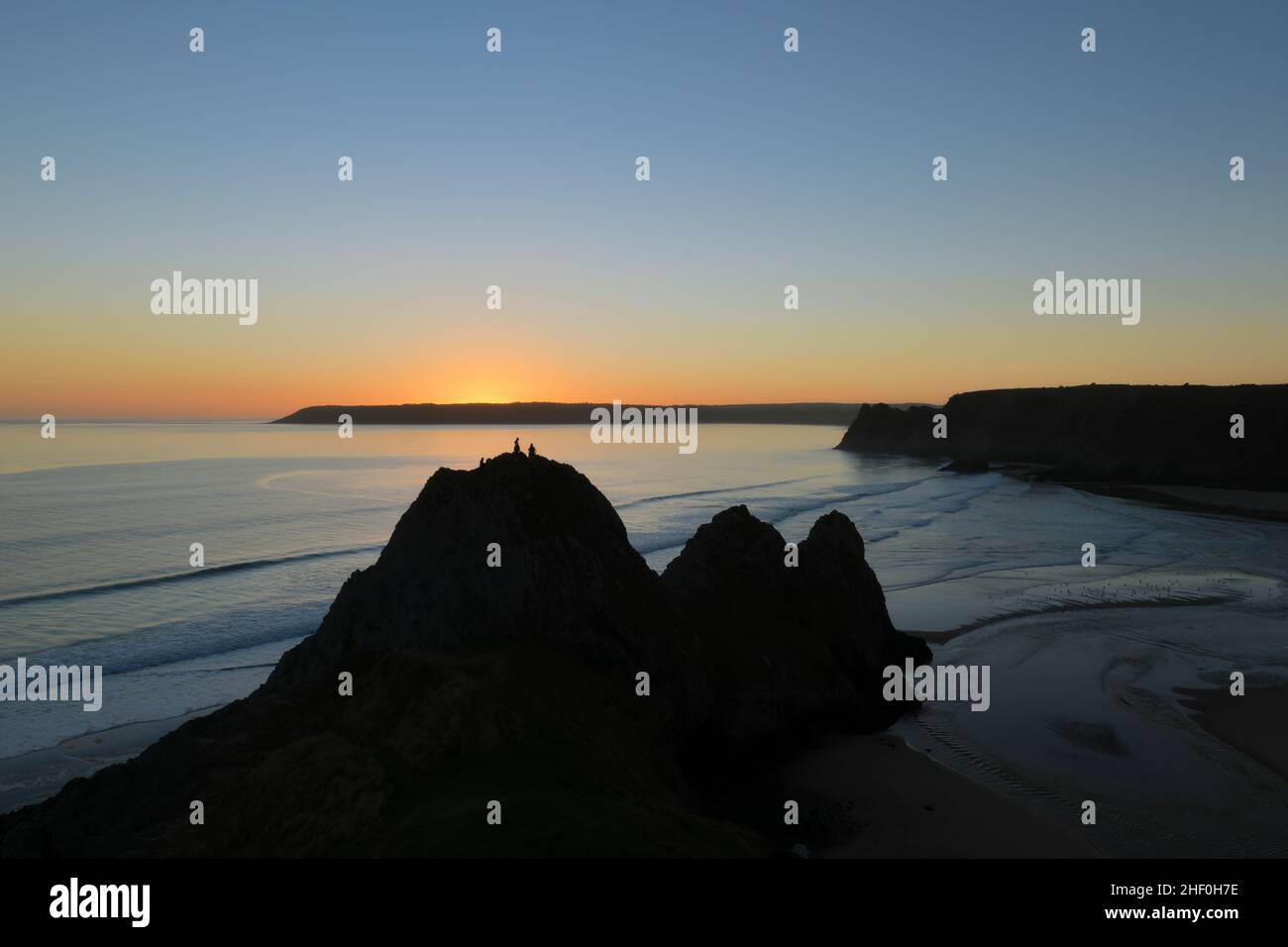 Climbers at the top of Three Cliffs bay with sun setting behind Oxwich ...
