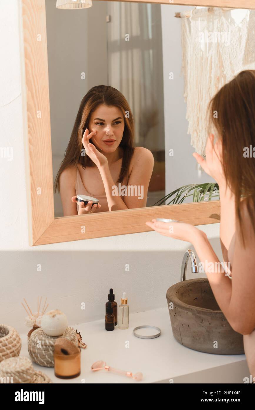A young woman applies moisturizer to her face in her sun bath. Daily ...