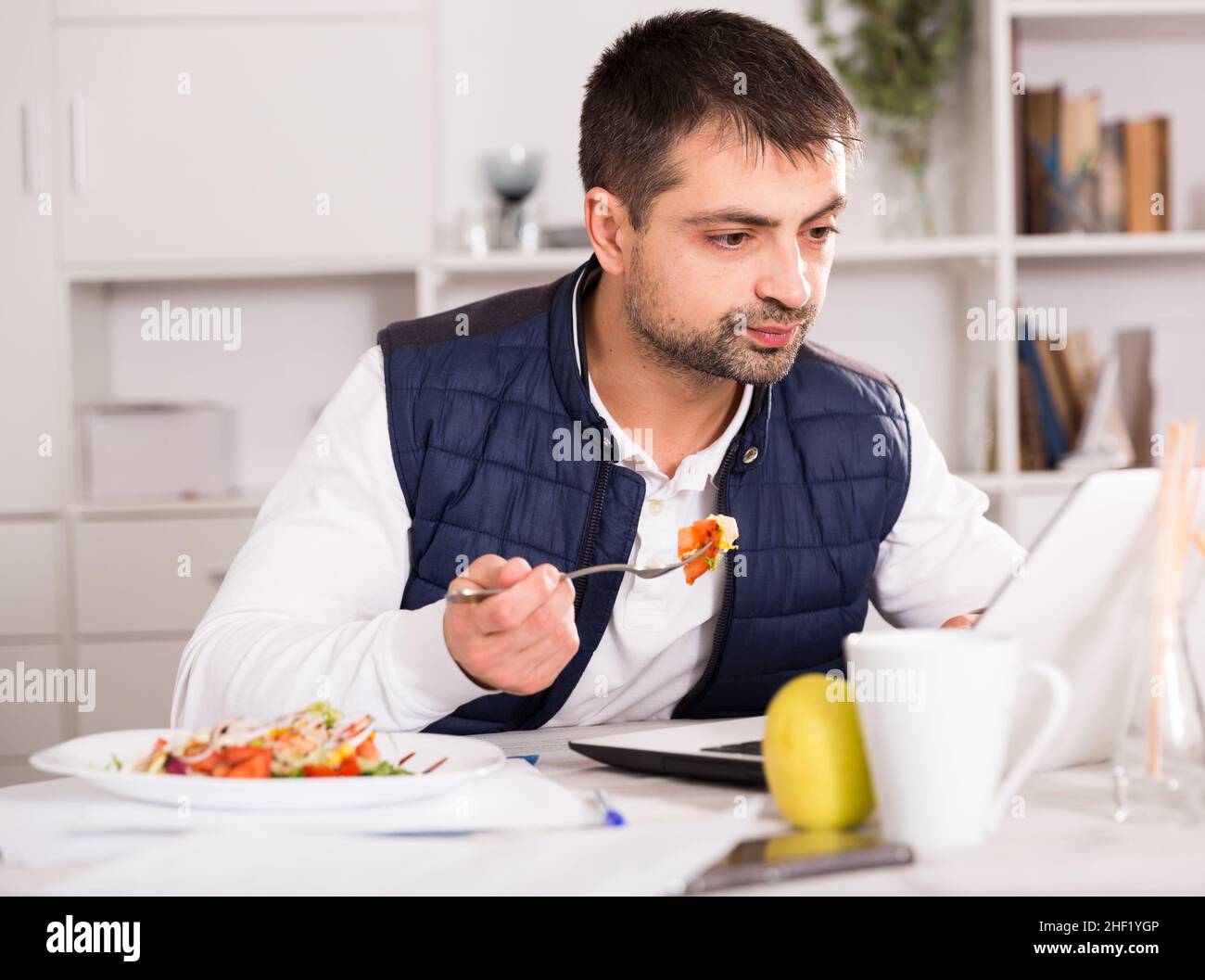 Positive young male holding fork, eating vegetable salad Stock Photo ...