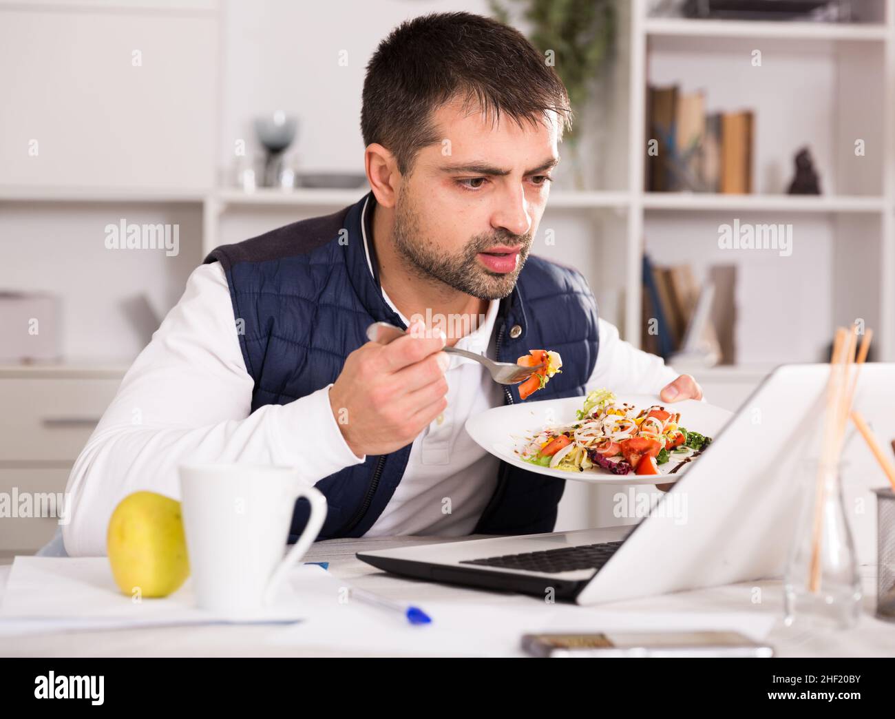 Positive young male holding fork, eating vegetable salad Stock Photo ...