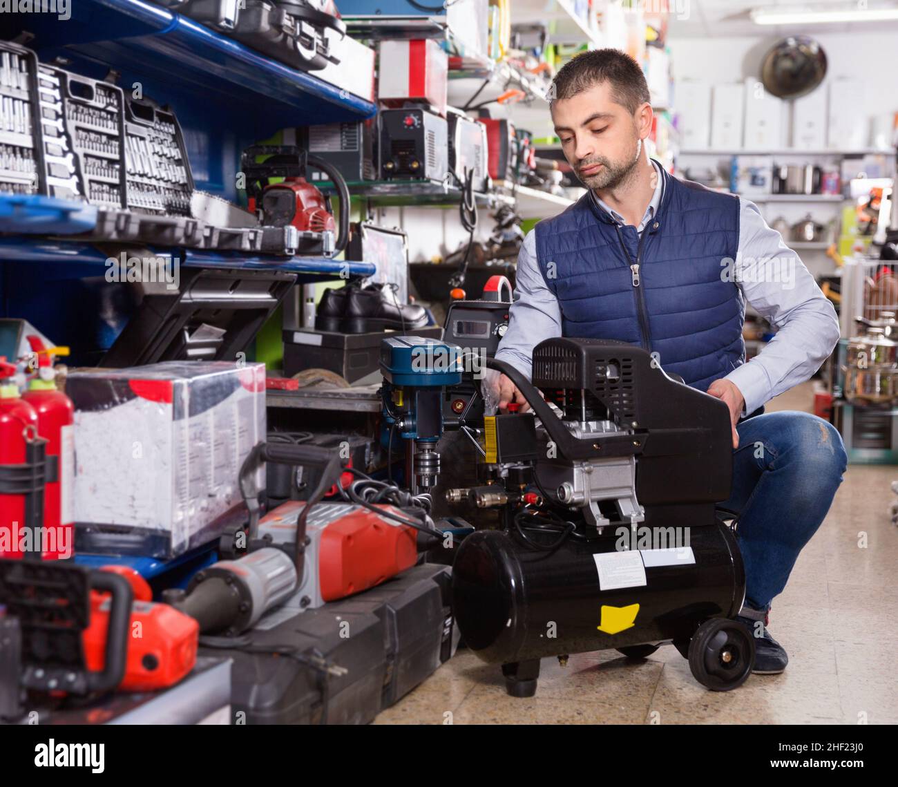 Adult male is standing with air compressor in tools store Stock Photo ...