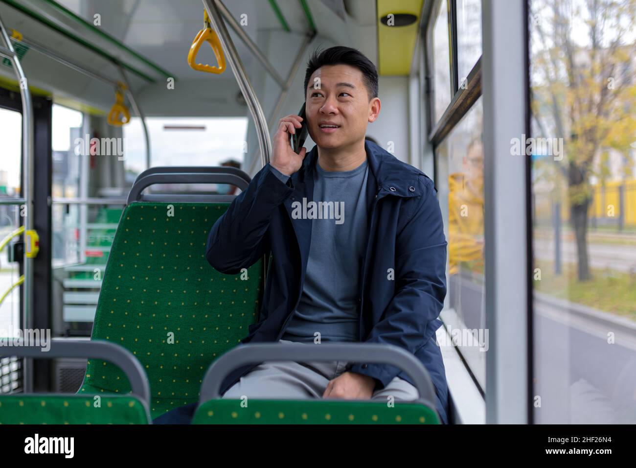asian man in public bus passenger having fun talking on mobile phone ...