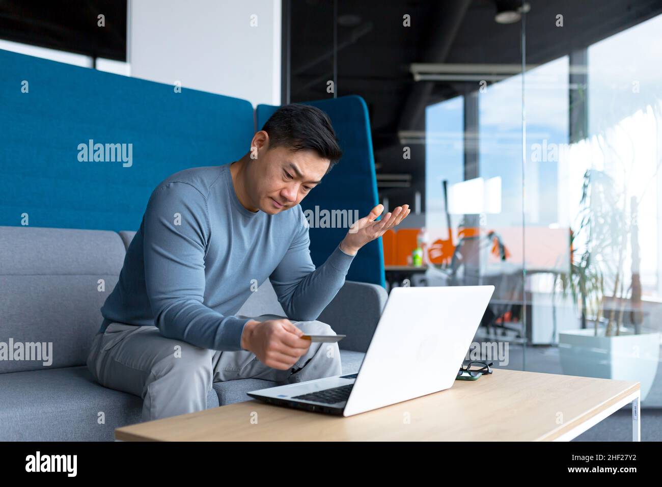 Annoyed and frustrated Asian man trying to make an online purchase ...