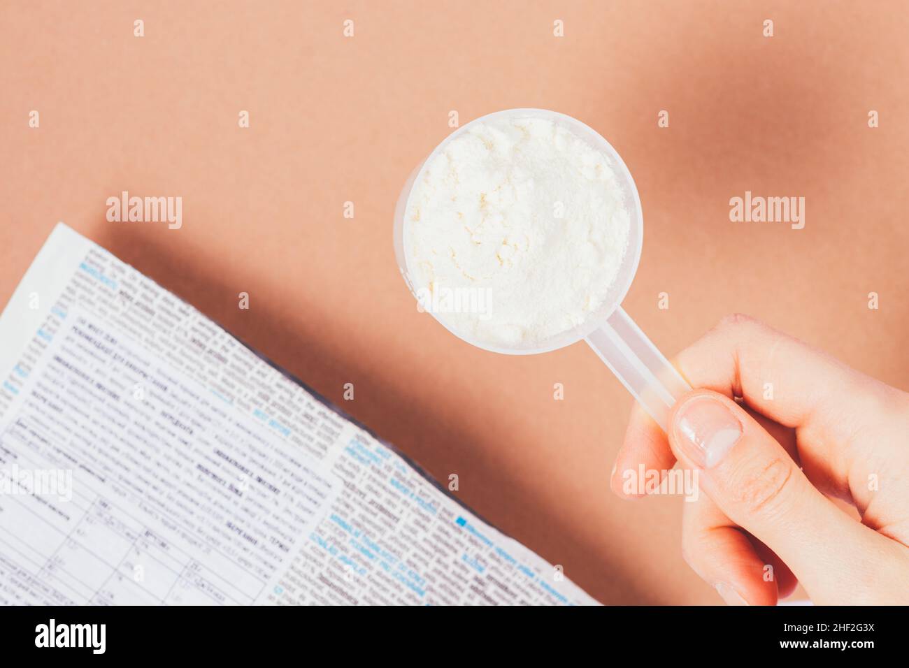 Scoop protein powder in woman's hand next to open pack of product on ...