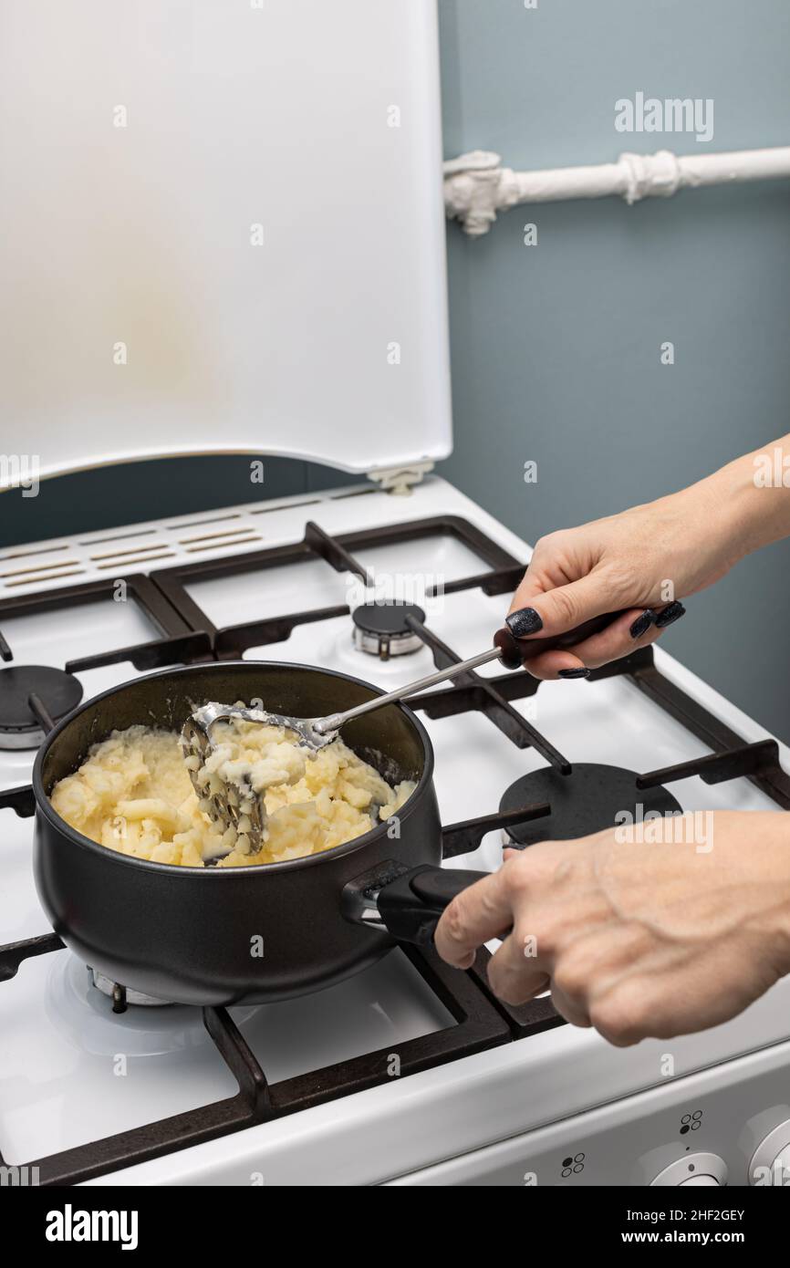 a woman's hand crumples boiled potatoes with a kitchen appliance. High ...