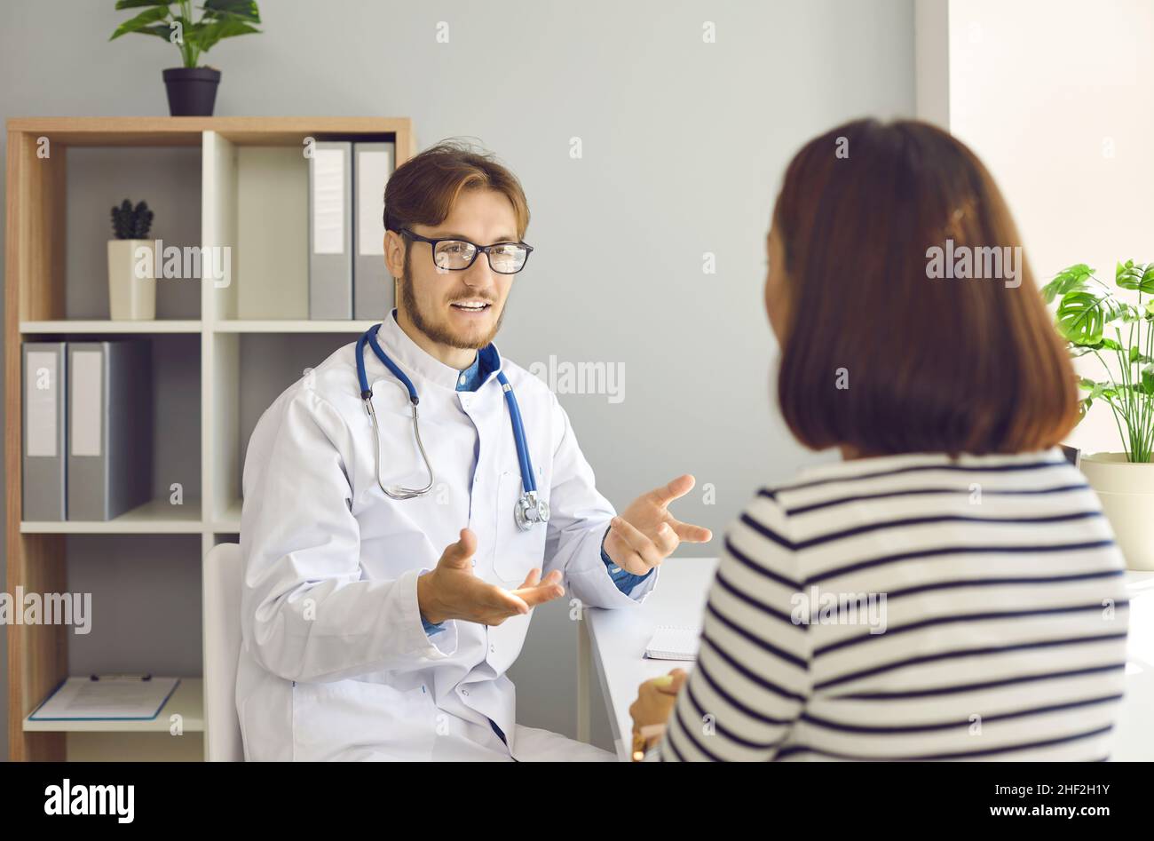 Doctor sitting at his desk and having discussion with patient who came ...
