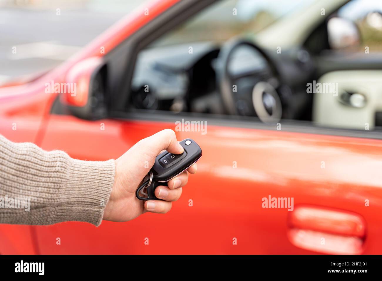 Male hand holding electronic remote key pushing button near red rental ...