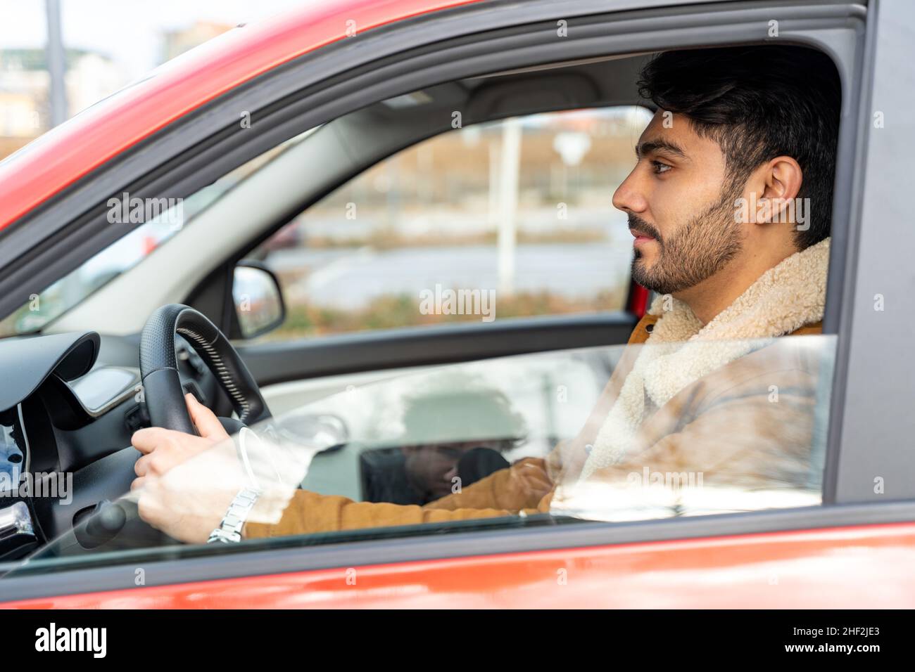 Man in jacket holding driving wheel riding car at daytime. View from ...