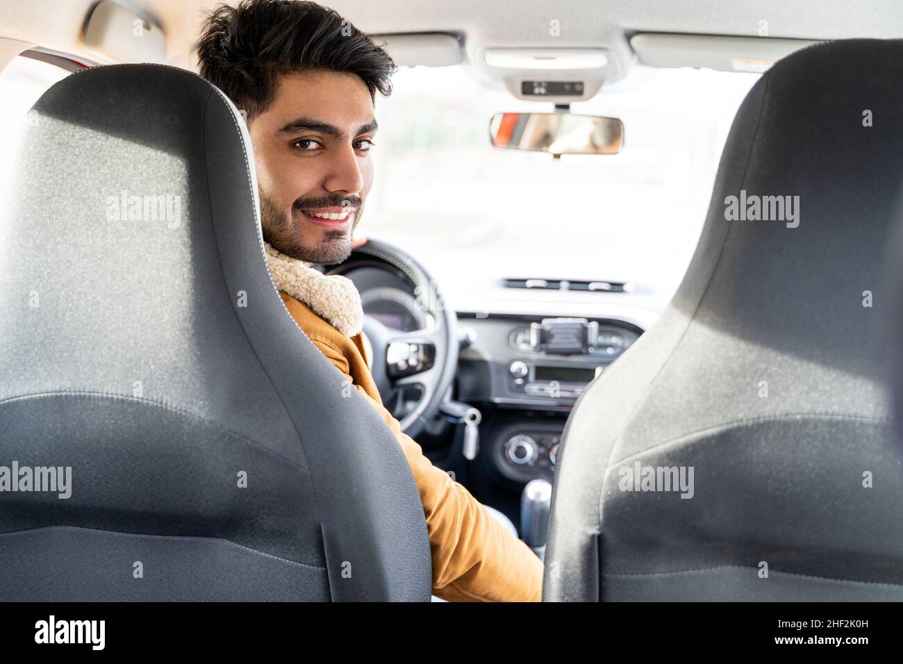 Man casually dressed with hand on driving wheel looking on backseat in ...